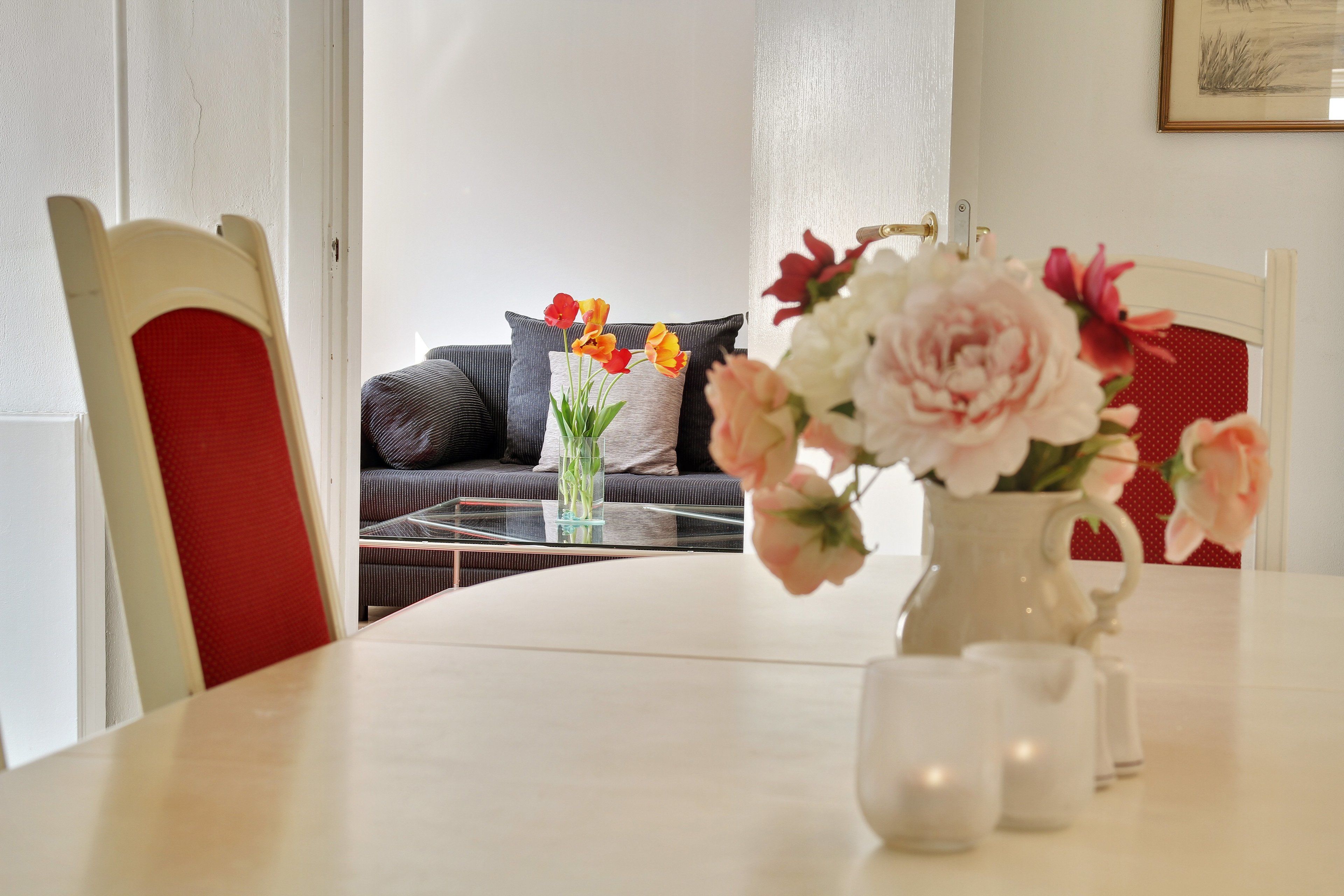 Uma mesa de jantar com um vaso de flores, uma mesa de centro de vidro e uma cadeira vermelha.