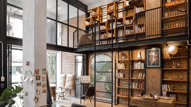 Um amplo loft com pé-alto, paredes de tijolo aparente e um mezanino com estantes de livros.