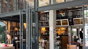 Um café moderno com fachada de vidro, mesas de madeira e um quadro de menu à vista.