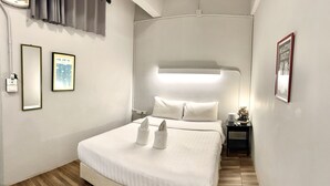 Quarto de hotel com uma cama, mesa de cabeceira, luminária na parede e um quadro emoldurado.