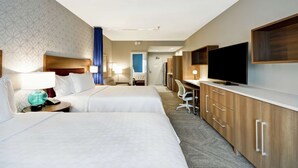 Quarto de hotel com duas camas, uma escrivaninha, uma televisão e um banheiro visível ao fundo.