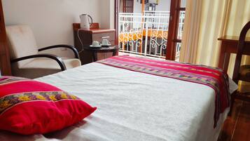 Quarto de hotel com cama, cadeira, uma pequena mesa com chaleira e varanda com guarda-corpo.