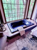 Quarto com uma banheira grande, janela com vista para árvores e um tapete no chão.