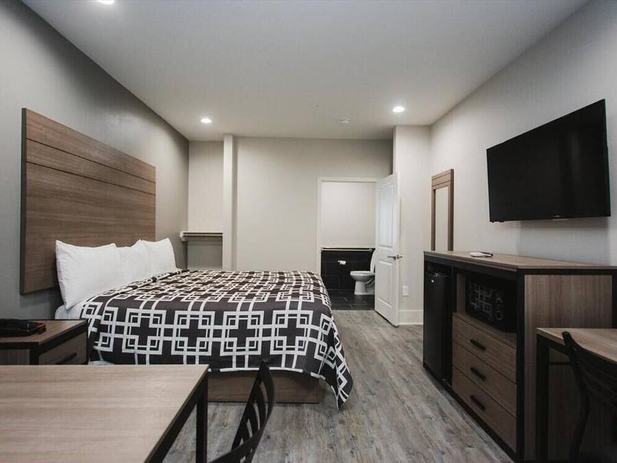 Quarto de hotel moderno com uma cama grande, uma escrivaninha, uma televisão de tela plana e um banheiro pequeno.