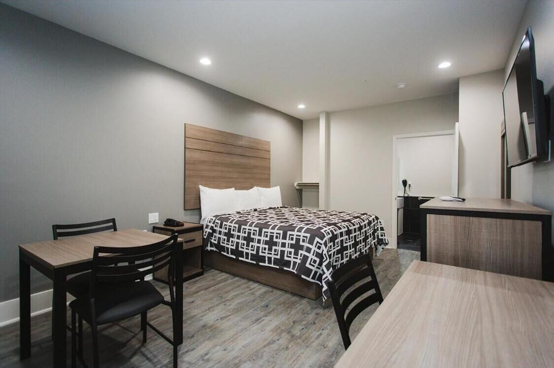 Quarto de hotel com cama, escrivaninha, cadeira e televisão.