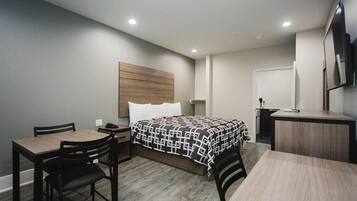 Quarto de hotel com cama, escrivaninha, cadeira e televisão.