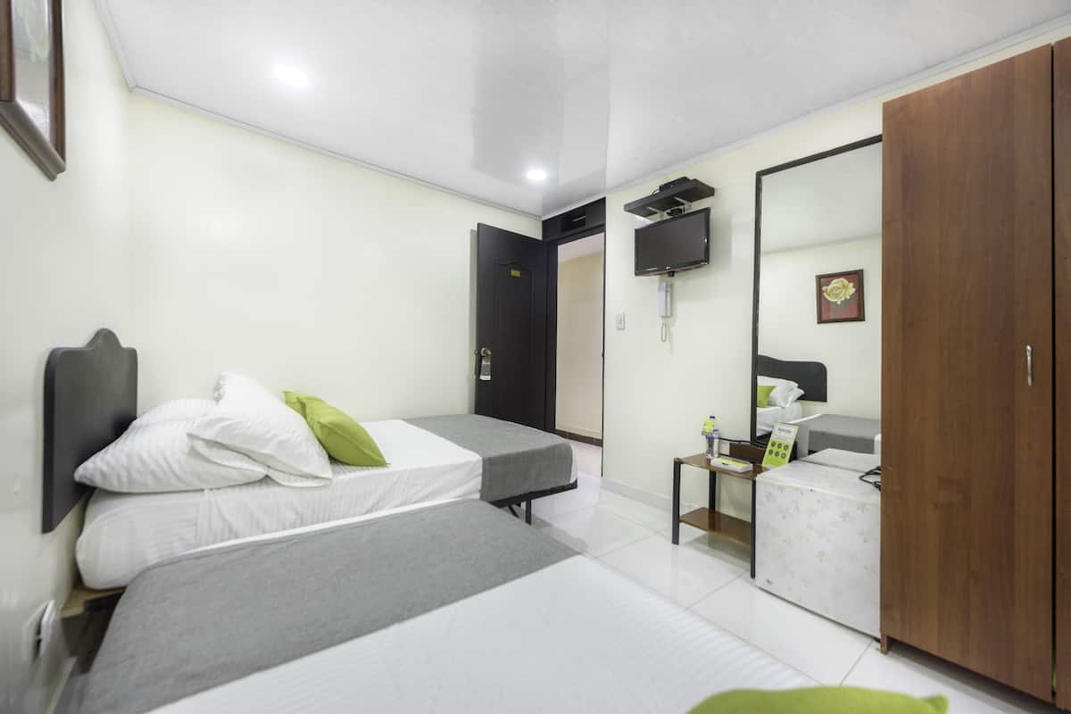 Quarto de hotel com duas camas, um guarda-roupa, uma televisão e uma pequena mesa com telefone.