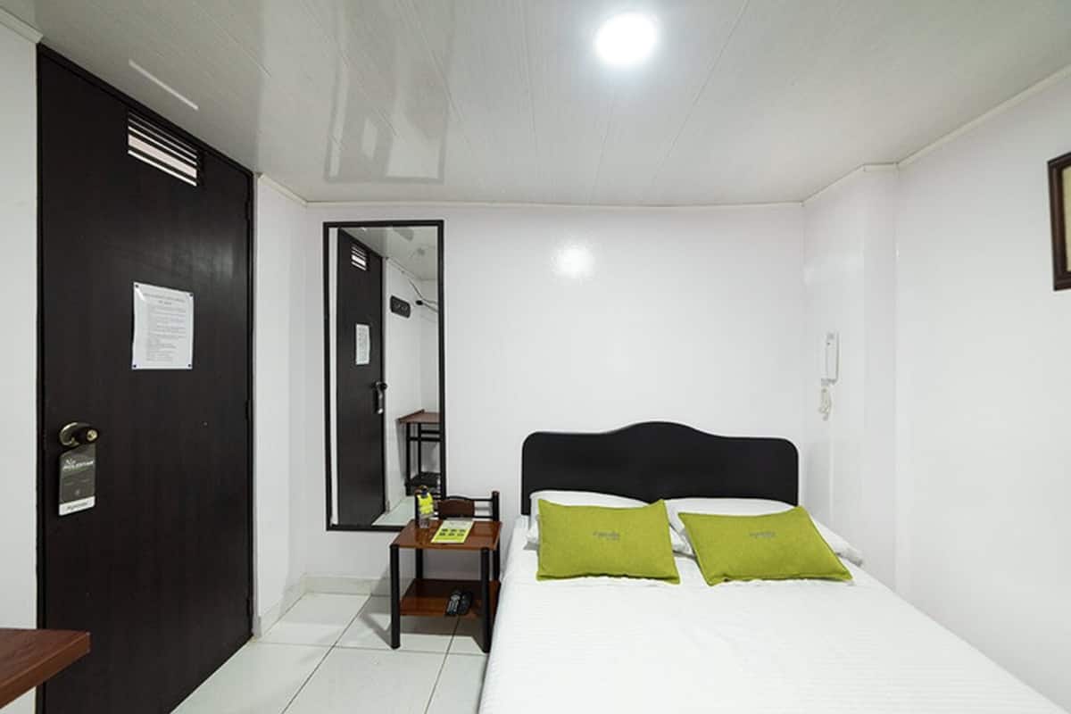 Quarto de hotel com uma cama, uma mesinha, um espelho e uma porta.