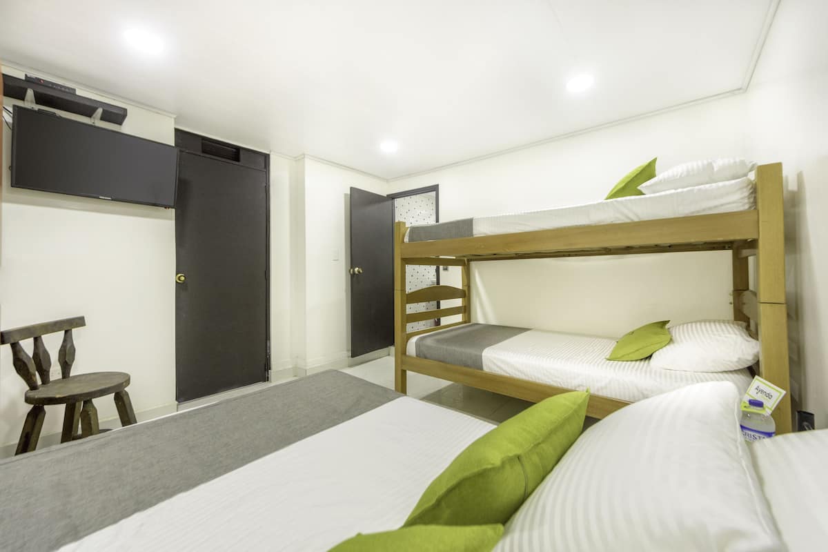 Quarto com beliche, escrivaninha, cadeira, televisão e porta.