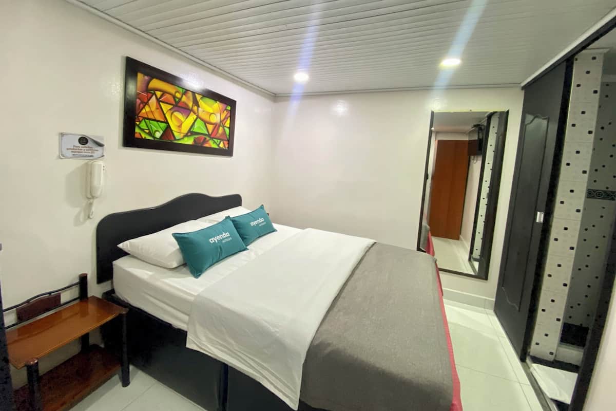 Quarto de hotel com cama, mesa de cabeceira, telefone, pintura na parede e espelho.