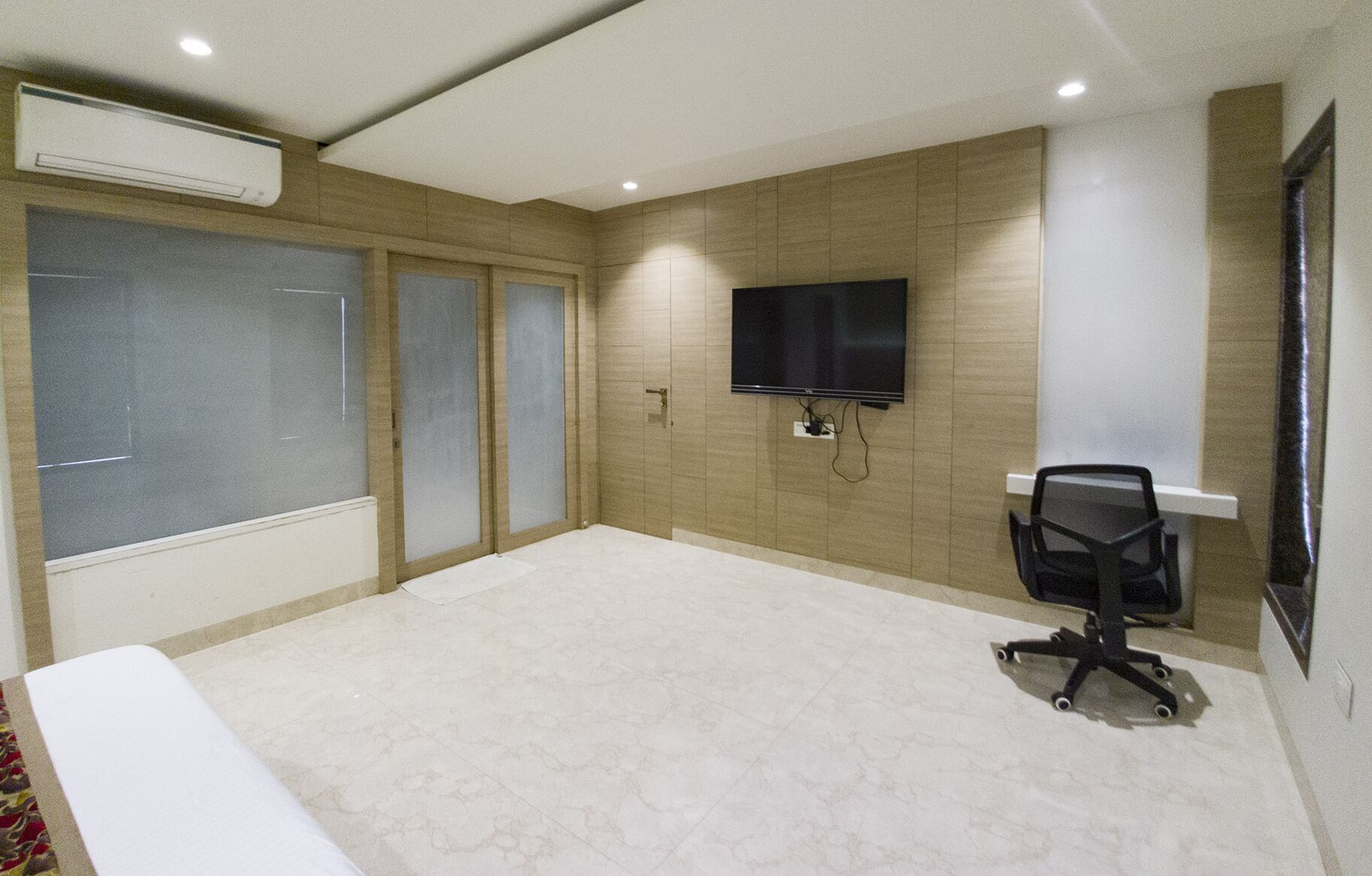 Quarto espaçoso com uma cama grande, televisão de tela plana na parede e uma cadeira.