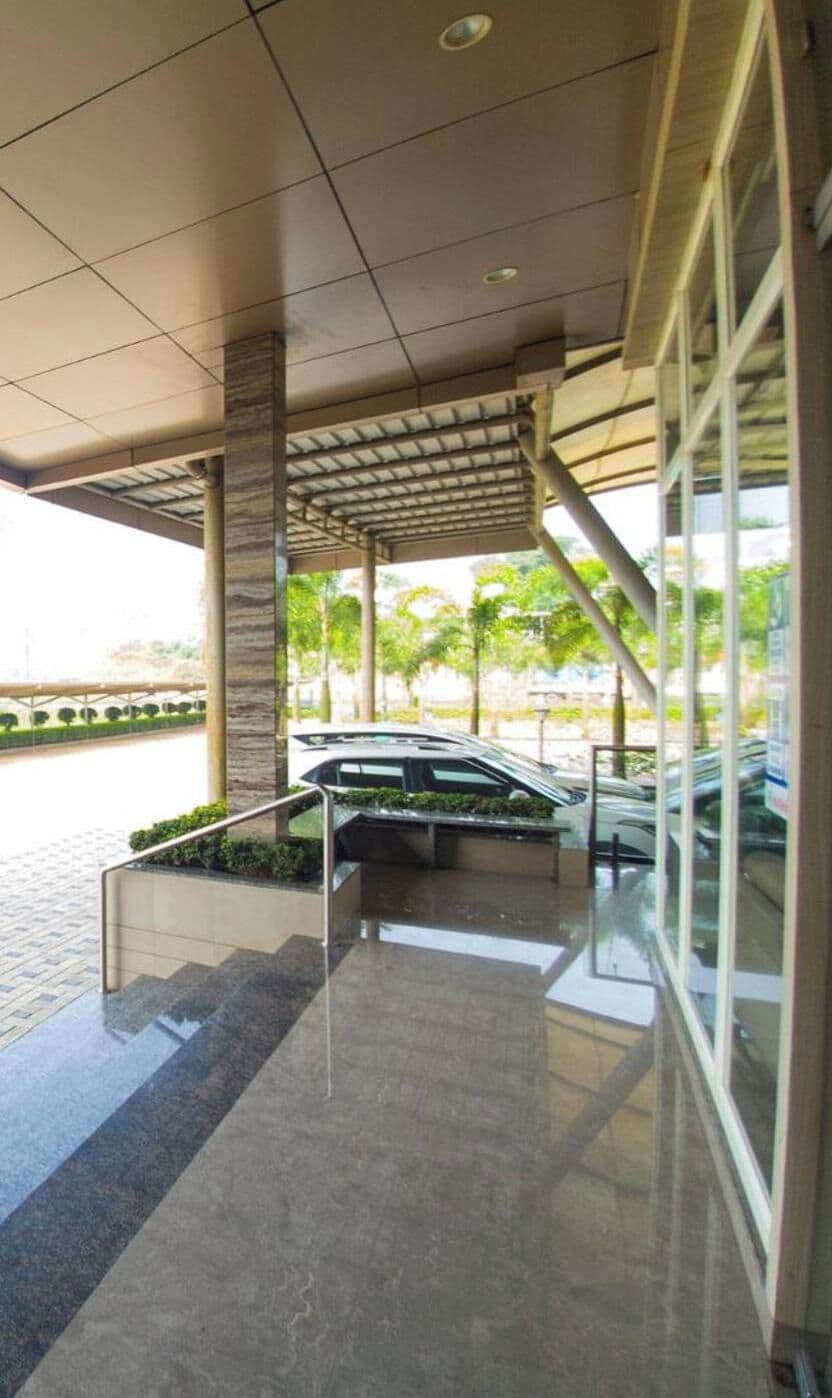 Área externa coberta com um carro estacionado, escadas descendo e vista da rua com carros e vegetação.