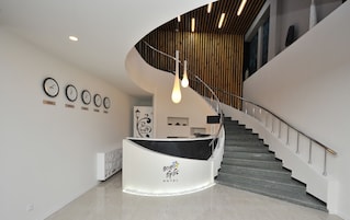 Uma área de recepção de hotel moderna, com um balcão curvo, uma escadaria e relógios fixados na parede.