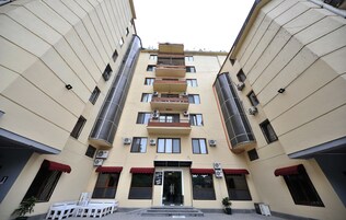 Um edifício com vários andares, entrada central, varandas e aparelhos de ar condicionado.