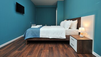 Quarto de hotel moderno com uma cama de solteiro, uma mesa de cabeceira com abajur e uma televisão de tela plana na parede.