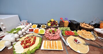 Uma mesa de buffet com diversos alimentos, incluindo queijos, carnes, frutas e legumes.