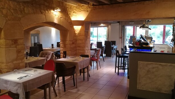 Restaurante com paredes de pedra, vigas de madeira e chão de azulejos. Mesas montadas com talheres e copos.