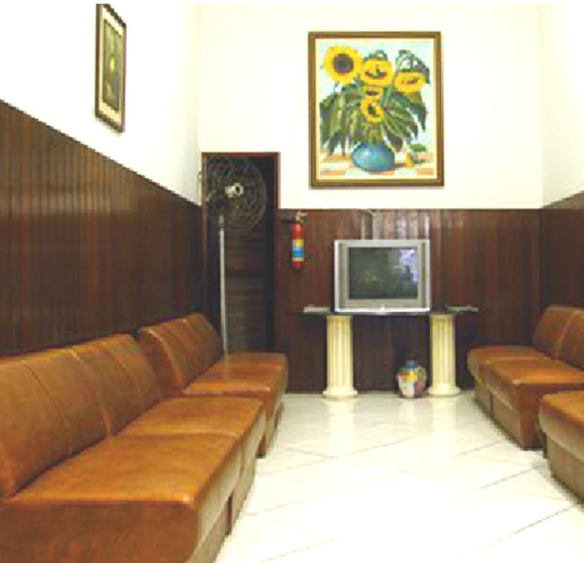 Um quarto com um sofá de couro marrom, uma televisão em um móvel e um quadro pendurado na parede.