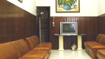 Um quarto com um sofá de couro marrom, uma televisão em um móvel e um quadro pendurado na parede.