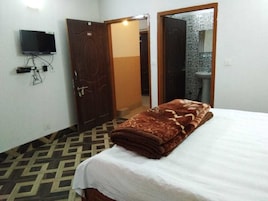 Quarto de hotel com uma cama, televisão fixada na parede e um banheiro visível através de uma porta aberta.