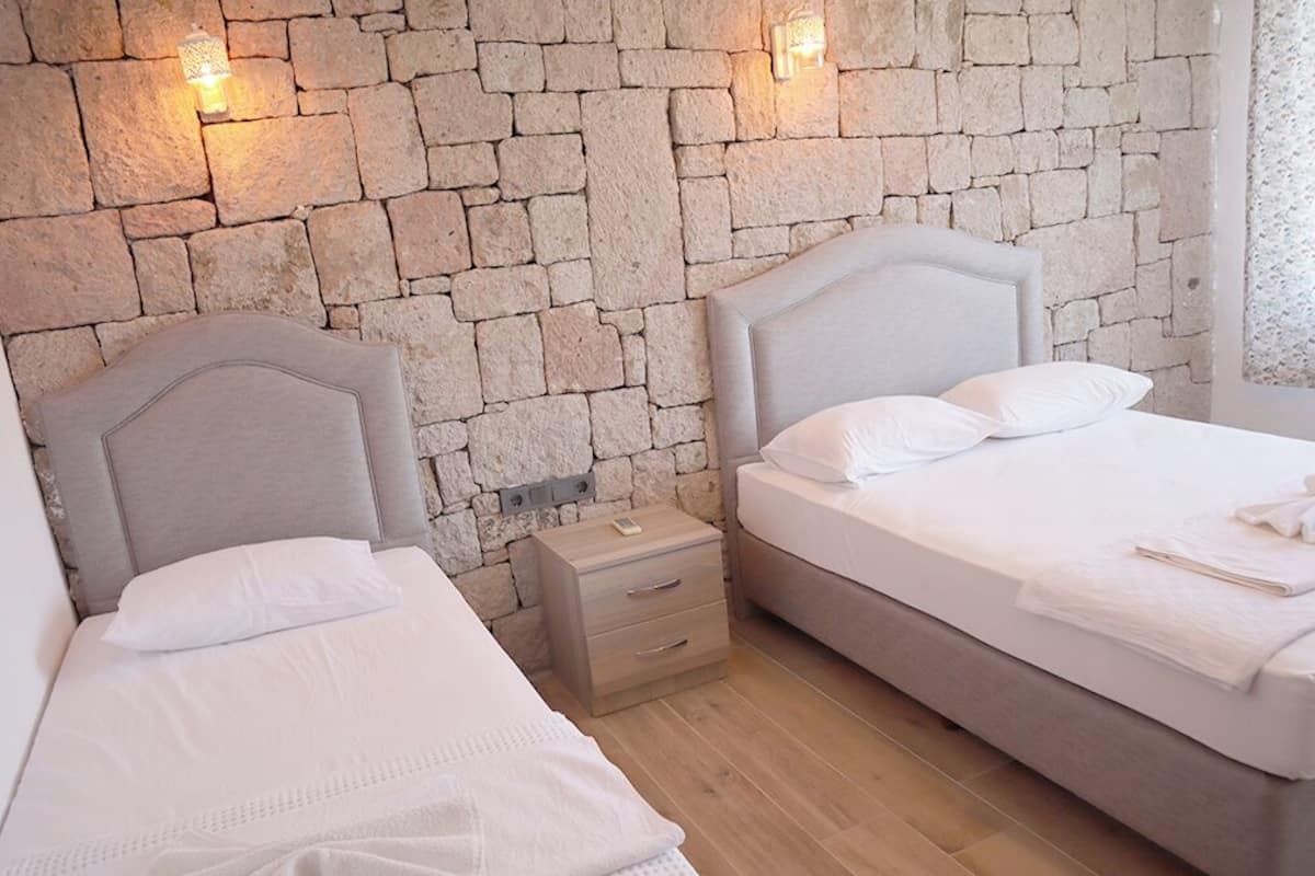 Quarto com duas camas, parede de pedra e mesa de cabeceira com abajur.