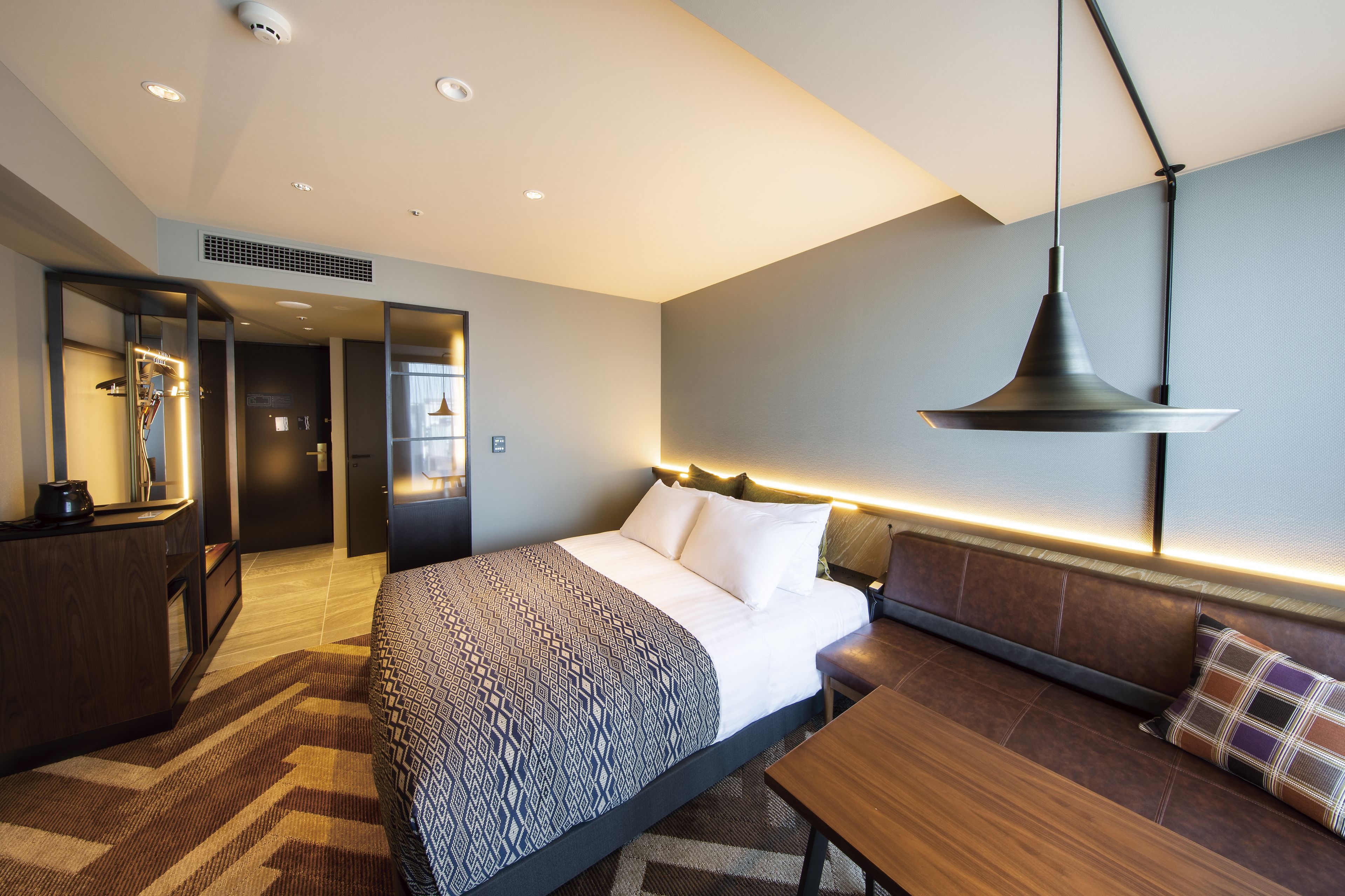 Quarto de hotel moderno com uma cama grande, um banco de madeira, uma escrivaninha e um espelho.