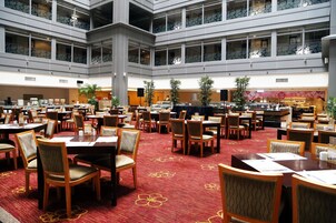 Um amplo hall de hotel com várias áreas de refeições, janelas grandes e um átrio central.