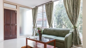 Uma sala de estar com um sofá verde, uma mesa de centro de madeira e uma janela grande com cortinas.