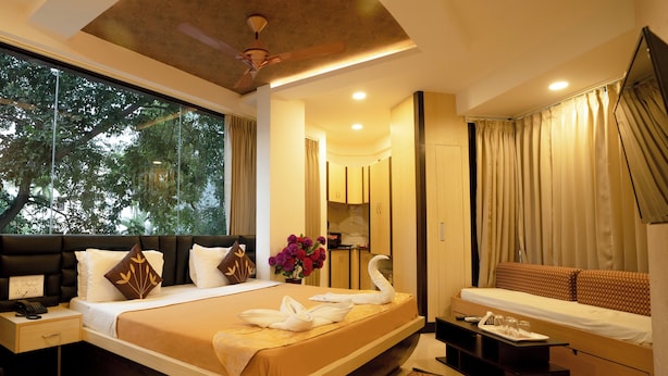 Quarto de hotel moderno com uma cama grande, um espaço de estar e vista para árvores pela janela.