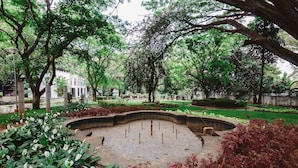 Um parque com uma fonte central, rodeado por diversas árvores e gramados bem cuidados.
