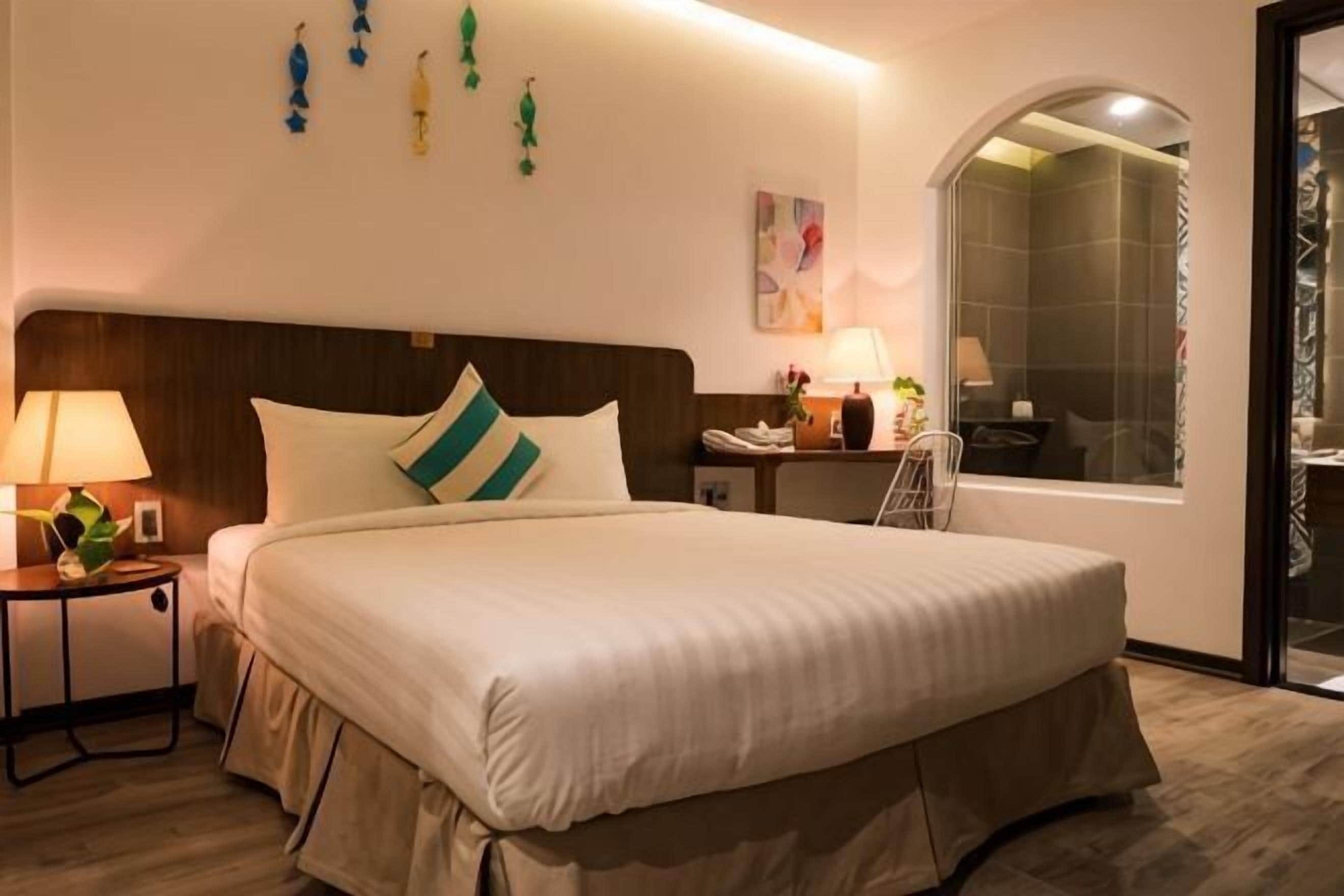 Quarto de hotel com cama, mesa de cabeceira, luminária e janela com vista.