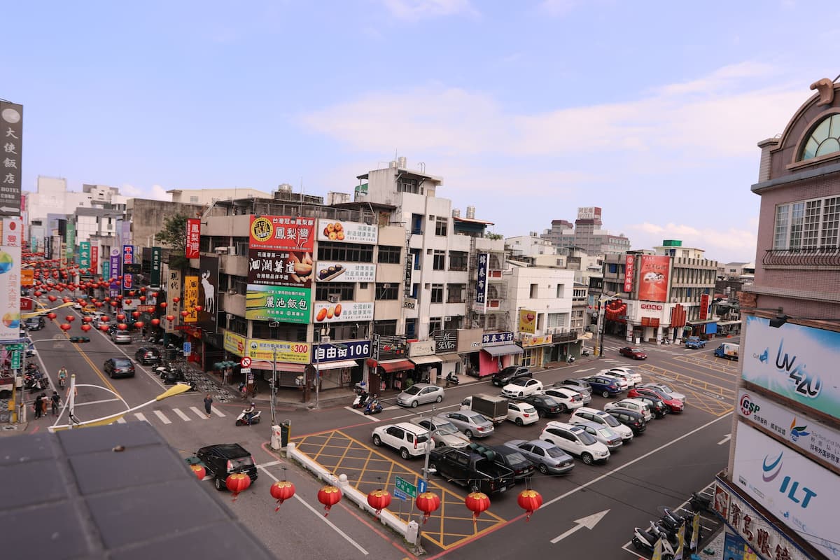Uma rua urbana movimentada com vários edifícios comerciais, incluindo um hotel com uma placa visível.