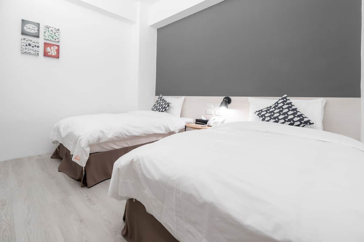 Quarto de hotel com duas camas, uma mesa de cabeceira com abajur, telefone e uma parede com quatro quadros emoldurados.