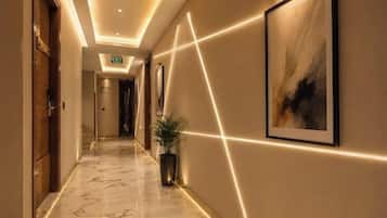Corredor de hotel com piso de mármore, quadros nas paredes e um vaso de planta.