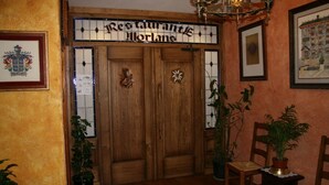 Uma porta de madeira com uma placa acima que diz "Restaurant Morlans". Há dois vasos de plantas de cada lado da porta.