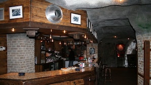 Um espaço de bar rústico com paredes de madeira, lareira de tijolos e teto de pedra.