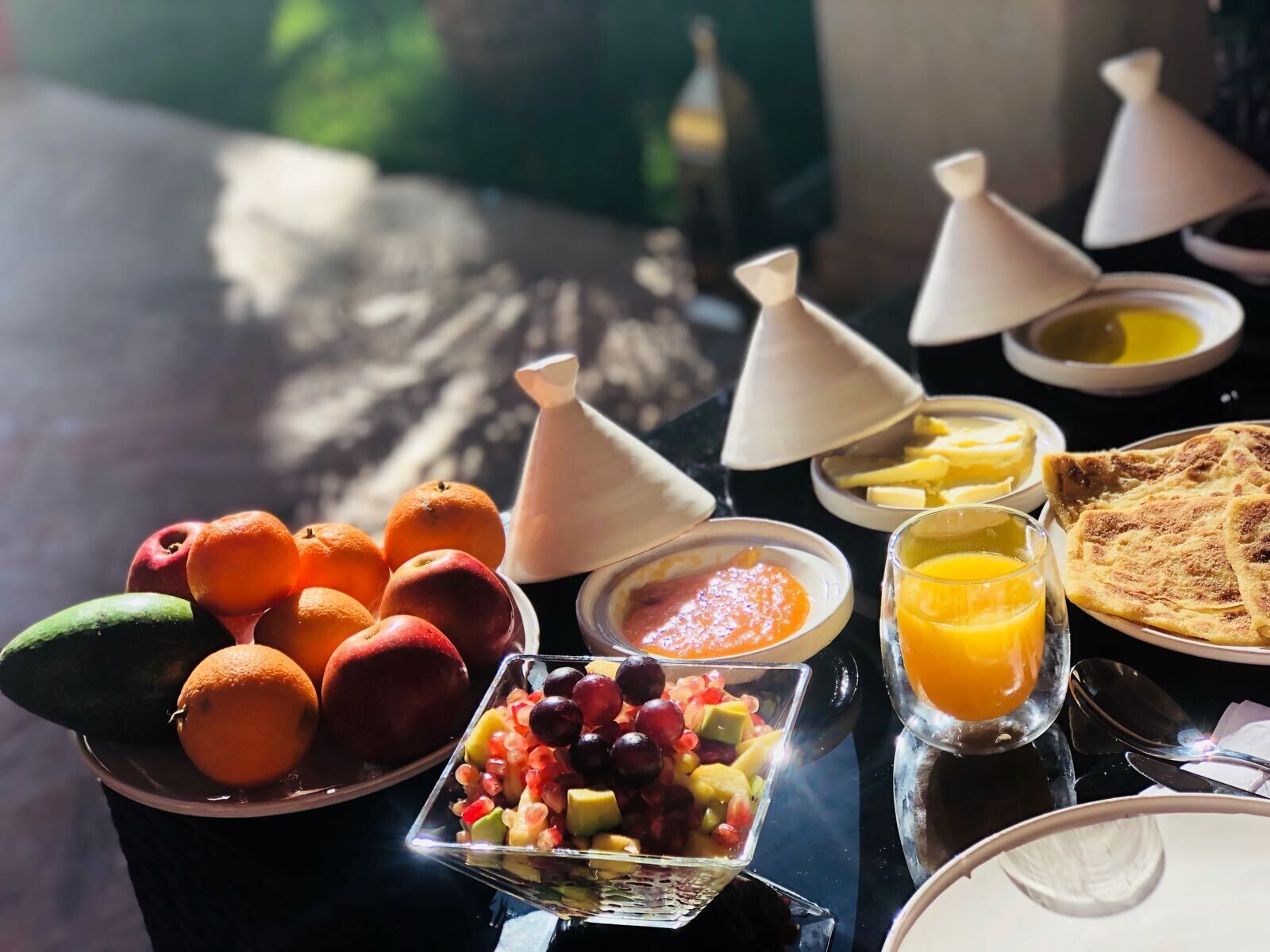 Mesa de café da manhã com frutas, um copo de suco de laranja e pratos típicos marroquinos.