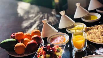 Mesa de café da manhã com frutas, um copo de suco de laranja e pratos típicos marroquinos.