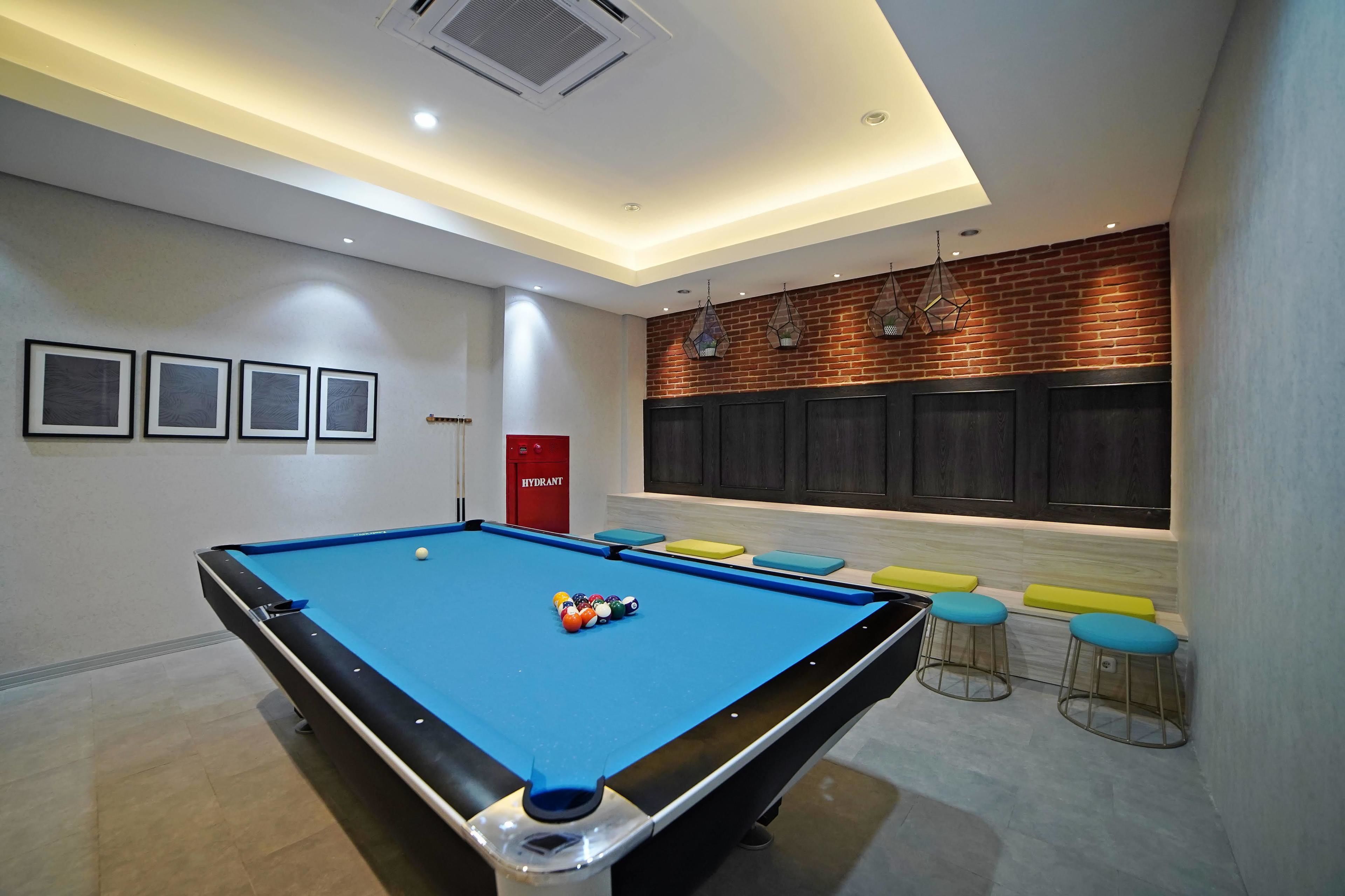 Mesa de bilhar com bolas, hidrante vermelho e banquetas de bar em um ambiente moderno com parede de tijolos e iluminação embutida.