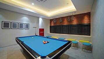 Mesa de bilhar com bolas, hidrante vermelho e banquetas de bar em um ambiente moderno com parede de tijolos e iluminação embutida.