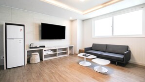Uma sala de estar moderna com televisão de tela plana, um sofá e duas mesinhas brancas.