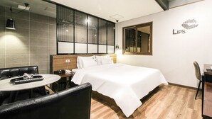 Quarto de hotel com uma cama, uma escrivaninha com cadeira, uma mesinha e um espelho na parede.