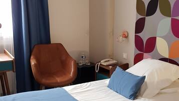 Quarto de hotel com duas camas, uma escrivaninha, uma cadeira, um telefone e uma decoração colorida na parede.