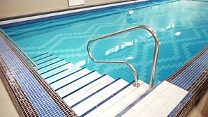 Piscina com escada de metal e degraus azulejados dando acesso à água.