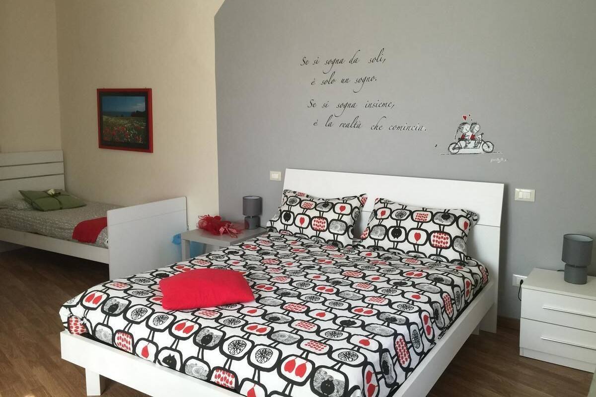 Um quarto com cama, mesas de cabeceira, relógio de parede e um quadro emoldurado.