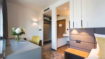 Quarto de hotel moderno com cama, mesa de cabeceira e escrivaninha com cadeira. Há um vaso com flores na escrivaninha.