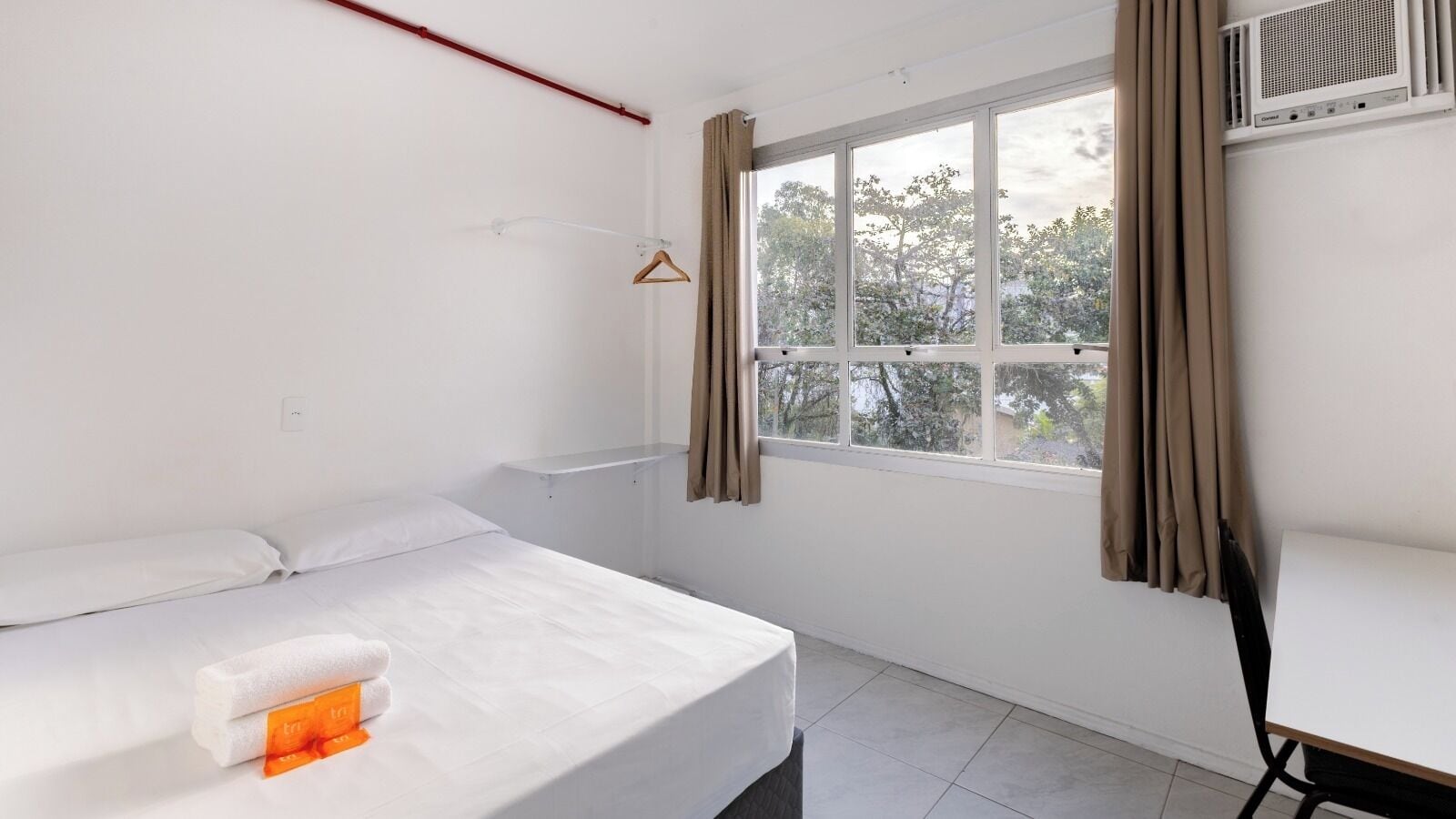 Quarto individual com janela, escrivaninha e cadeira.