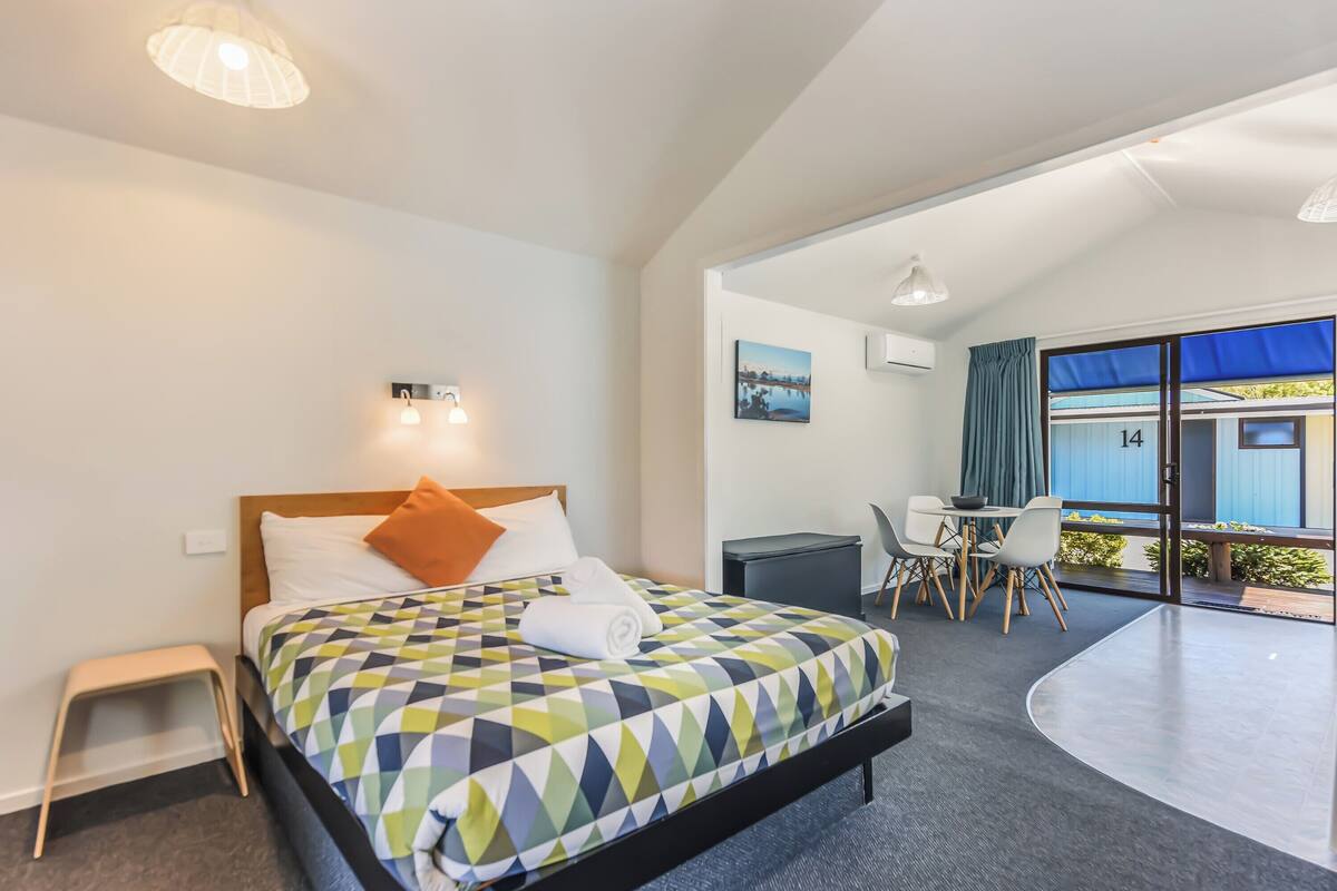Quarto de hotel moderno com cama, uma pequena mesa de escritório, uma cadeira e varanda com vista.