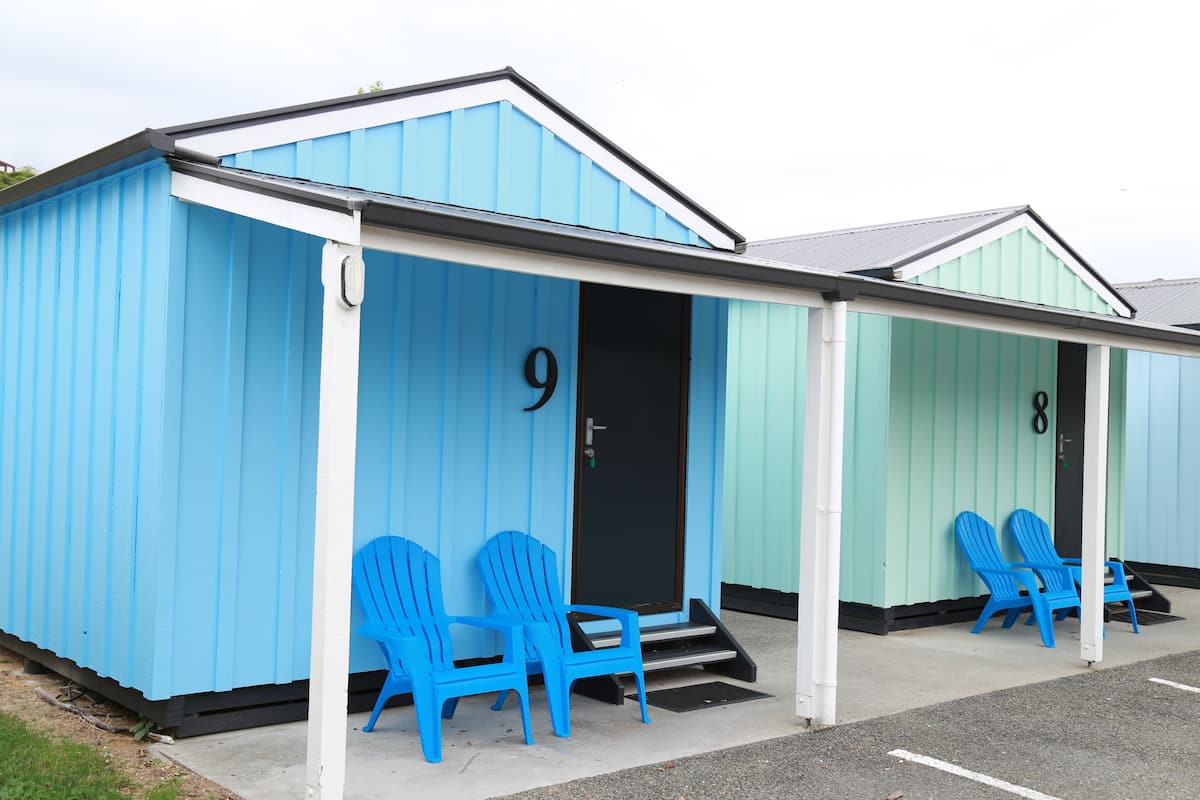 Um motel com quartos numerados, cada um com uma varanda e duas cadeiras azuis.