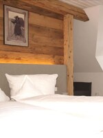 Quarto com teto de madeira, cama com roupa de cama branca e um quadro na parede.